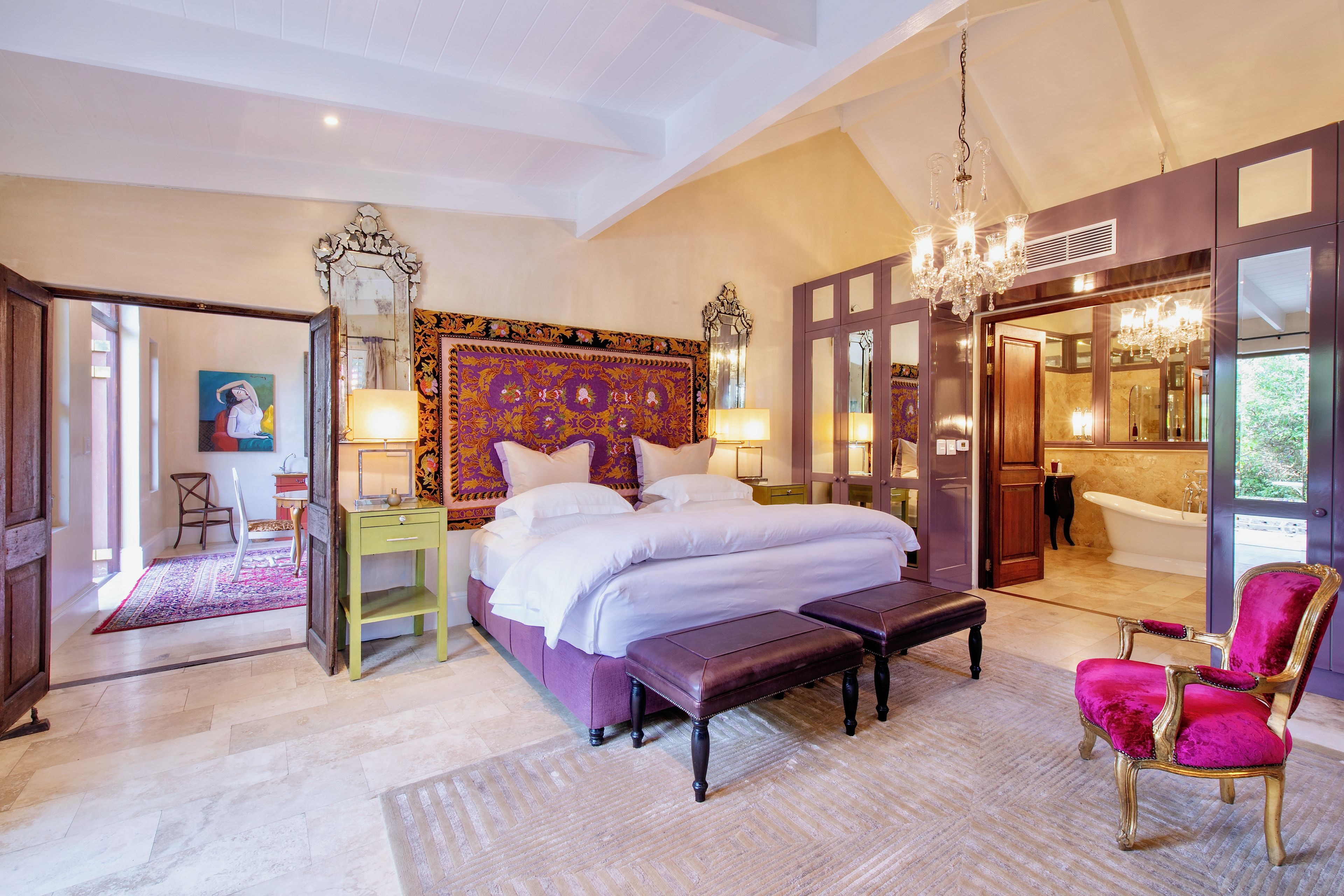 Um quarto espaçoso com uma cama grande, um banquinho, uma toucador e um banheiro visível por uma porta aberta.