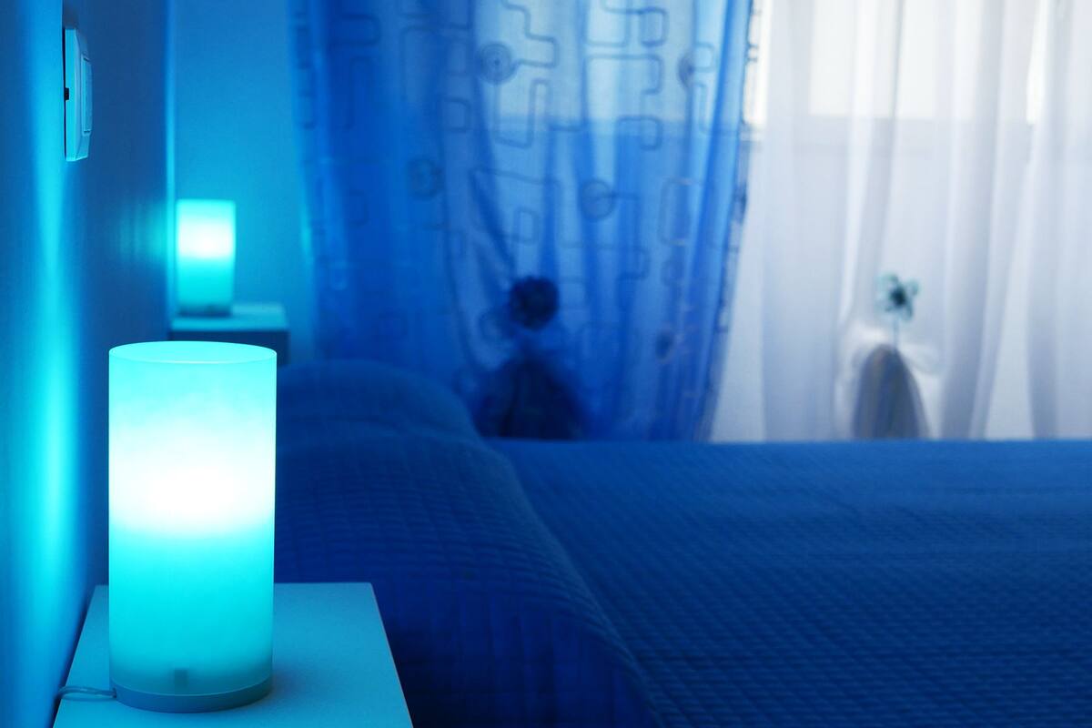 Quarto com cama, luminária de cabeceira e janela com cortinas.