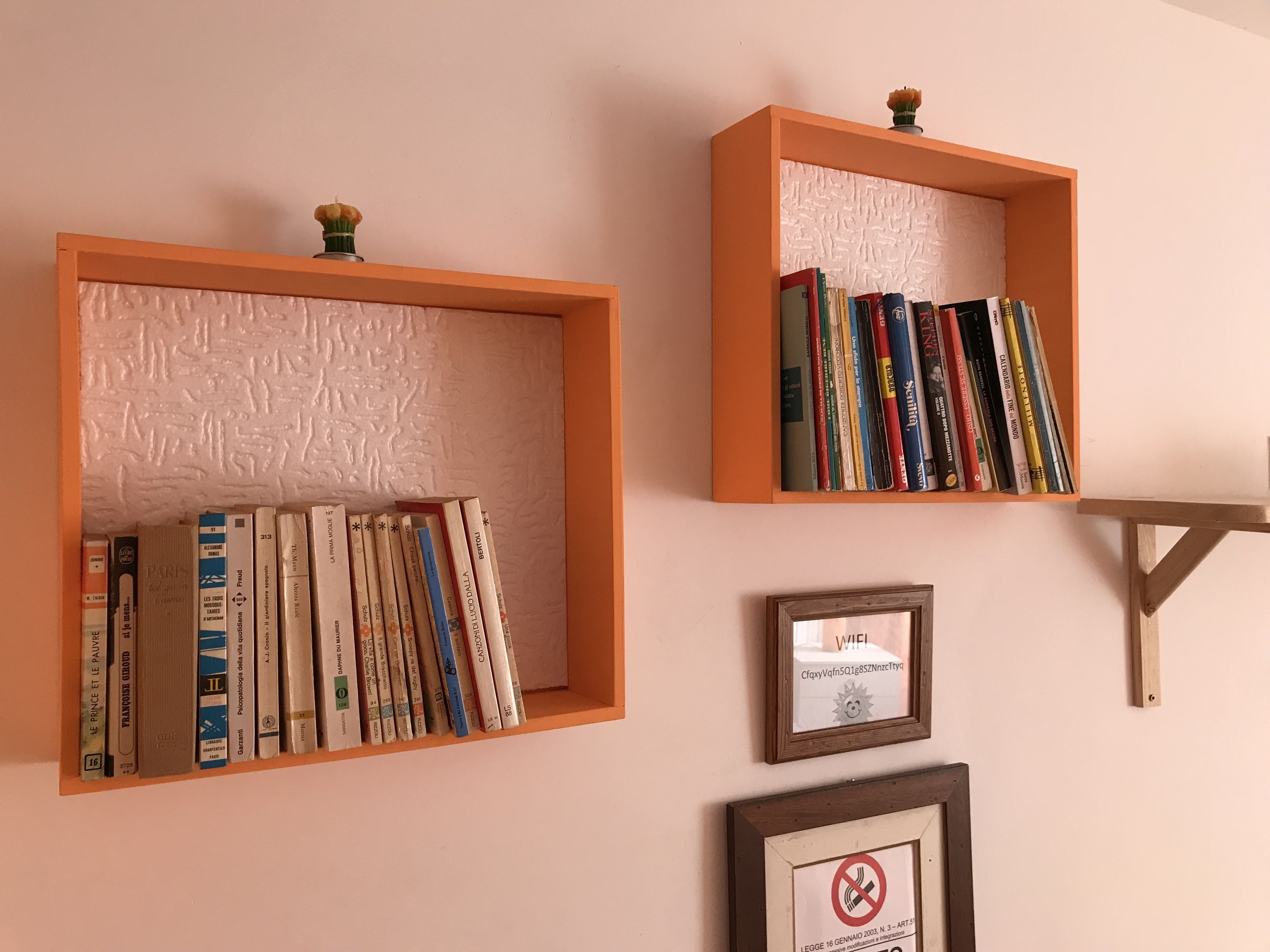 Duas estantes de madeira encostadas a uma parede, cada uma com livros e um pequeno objeto decorativo.