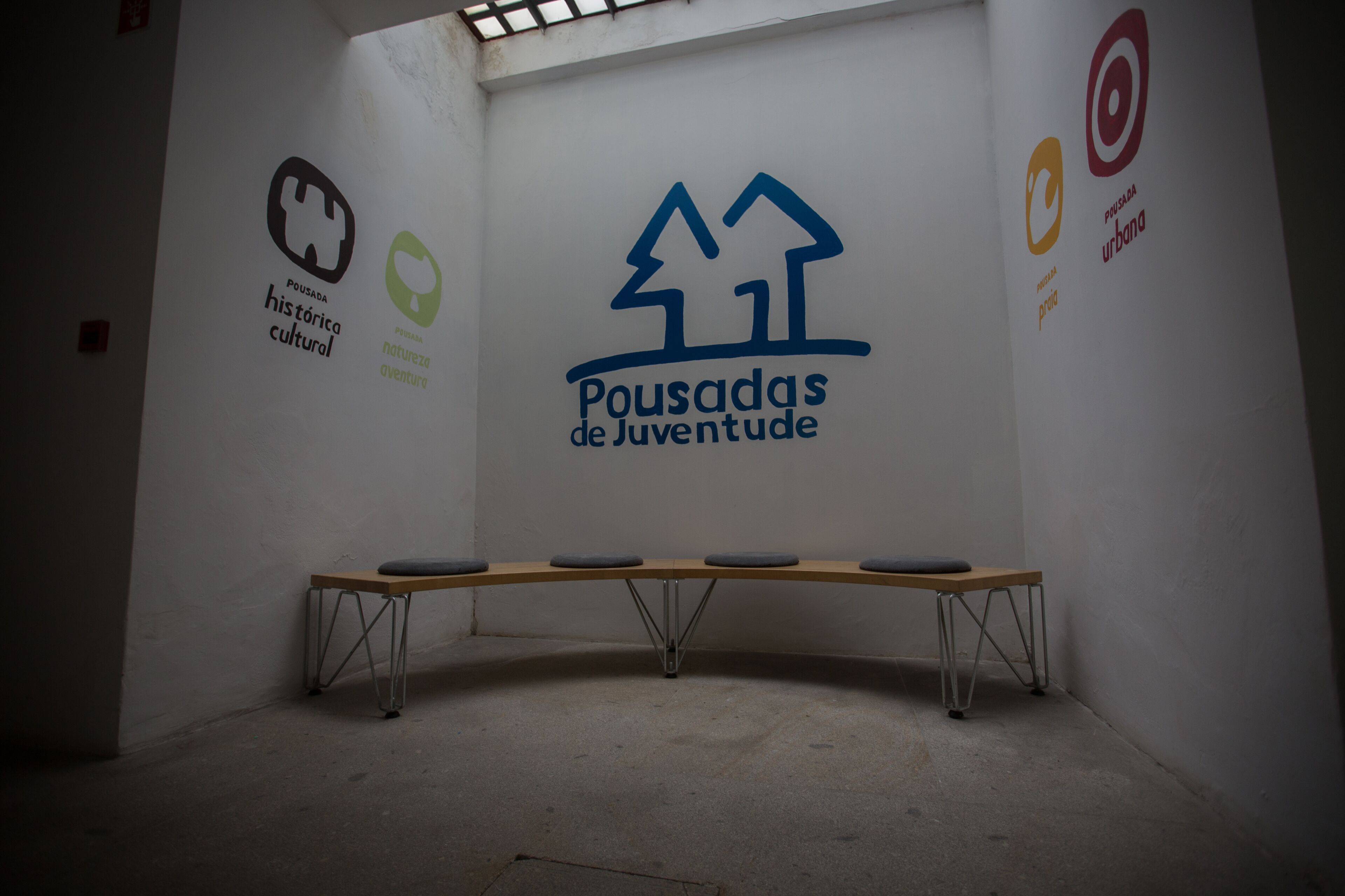 Uma sala de conferências com uma mesa comprida e cadeiras, um quadro branco com logotipos e uma parede lisa.