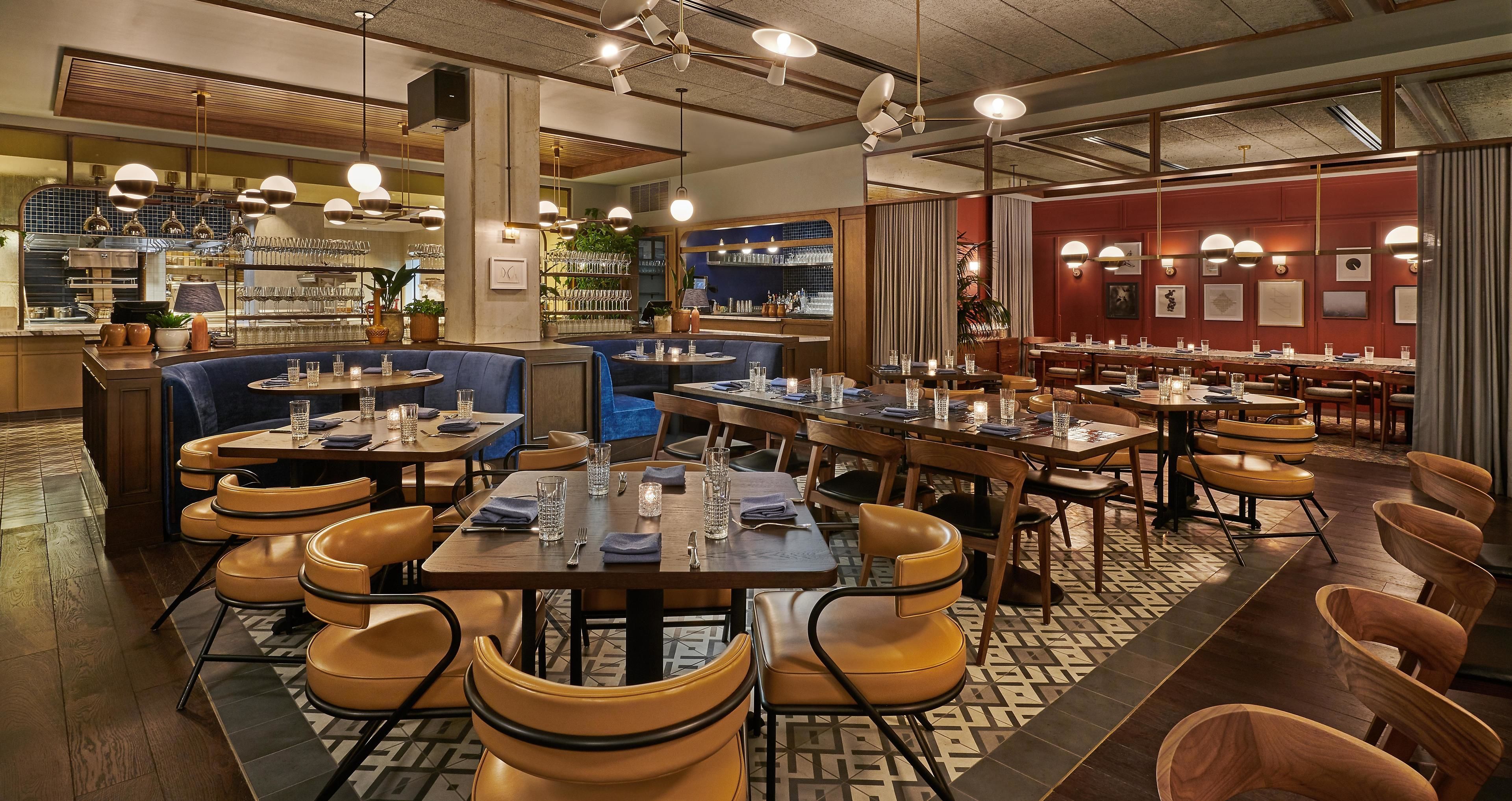 Interior de restaurante com várias mesas e cadeiras para refeições, um bar e cozinha ao fundo.