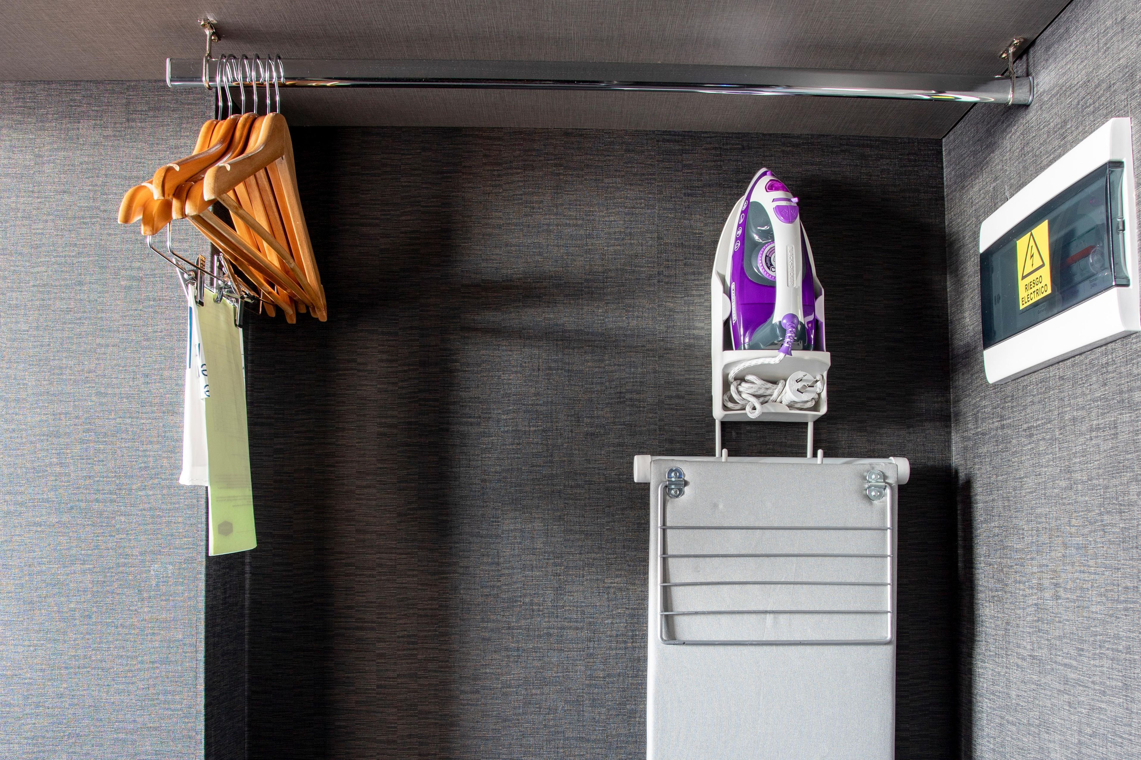 Quarto com uma estante de metal para roupas, um eletrodoméstico branco com topo roxo e um aviso de segurança na parede.