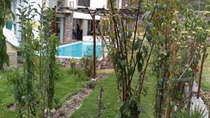 Uma casa moderna com piscina, cercada por um jardim bem cuidado com diversas plantas e vista clara para as montanhas ao fundo.