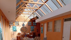 Quarto de hotel com teto alto, claraboia, área de refeições com mesa e cadeiras, e piso estampado.