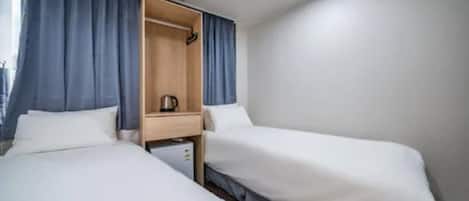 Quarto de hotel com duas camas, um guarda-roupa de madeira e uma pequena cozinha equipada.