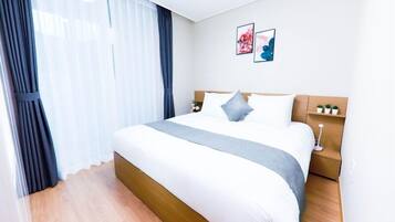 Quarto de hotel moderno com uma cama grande, cabeceira de madeira, mesas de cabeceira e uma pequena planta no criado-mudo.