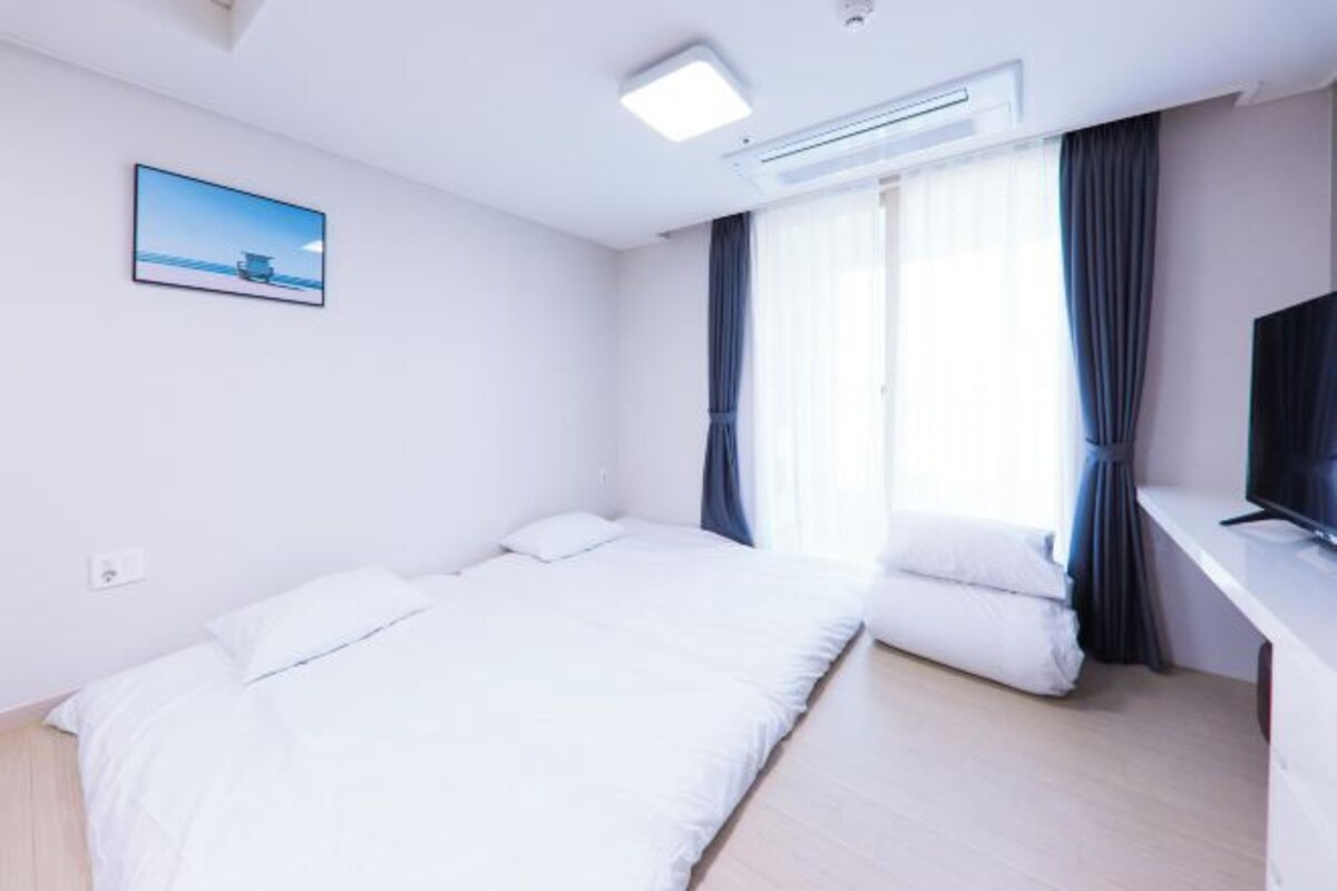 Quarto de hotel com cama, televisão de tela plana, janela com cortinas e um quadro na parede.