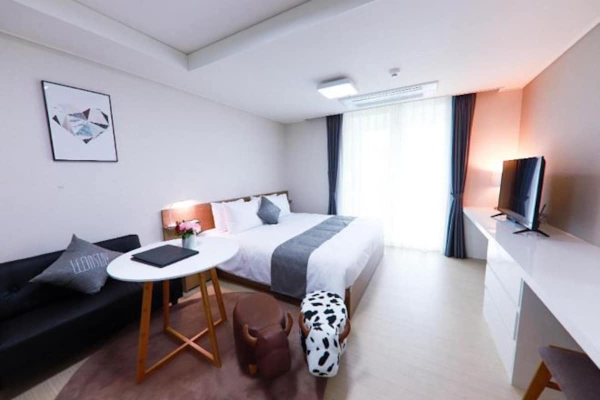 Quarto de hotel moderno com uma cama, uma mesa, uma televisão e uma pequena mesa.