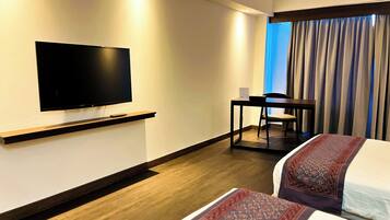 Quarto de hotel com televisão de tela plana na parede, uma escrivaninha com cadeira e uma cama com colcha estampada.