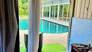 Quarto de hotel com cama, vista para uma piscina e área externa coberta.