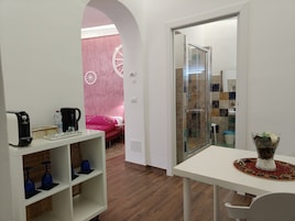 Quarto moderno com uma mesa branca, box de chuveiro de vidro, parede rosa e piso de madeira.
