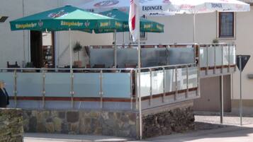 Restaurante com mesas ao ar livre, paredes de pedra e guarda-sóis com logotipos.