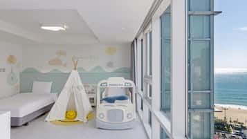 Quarto de criança com beliche, uma tenda de brincar, um ônibus de brinquedo e vista para o oceano.
