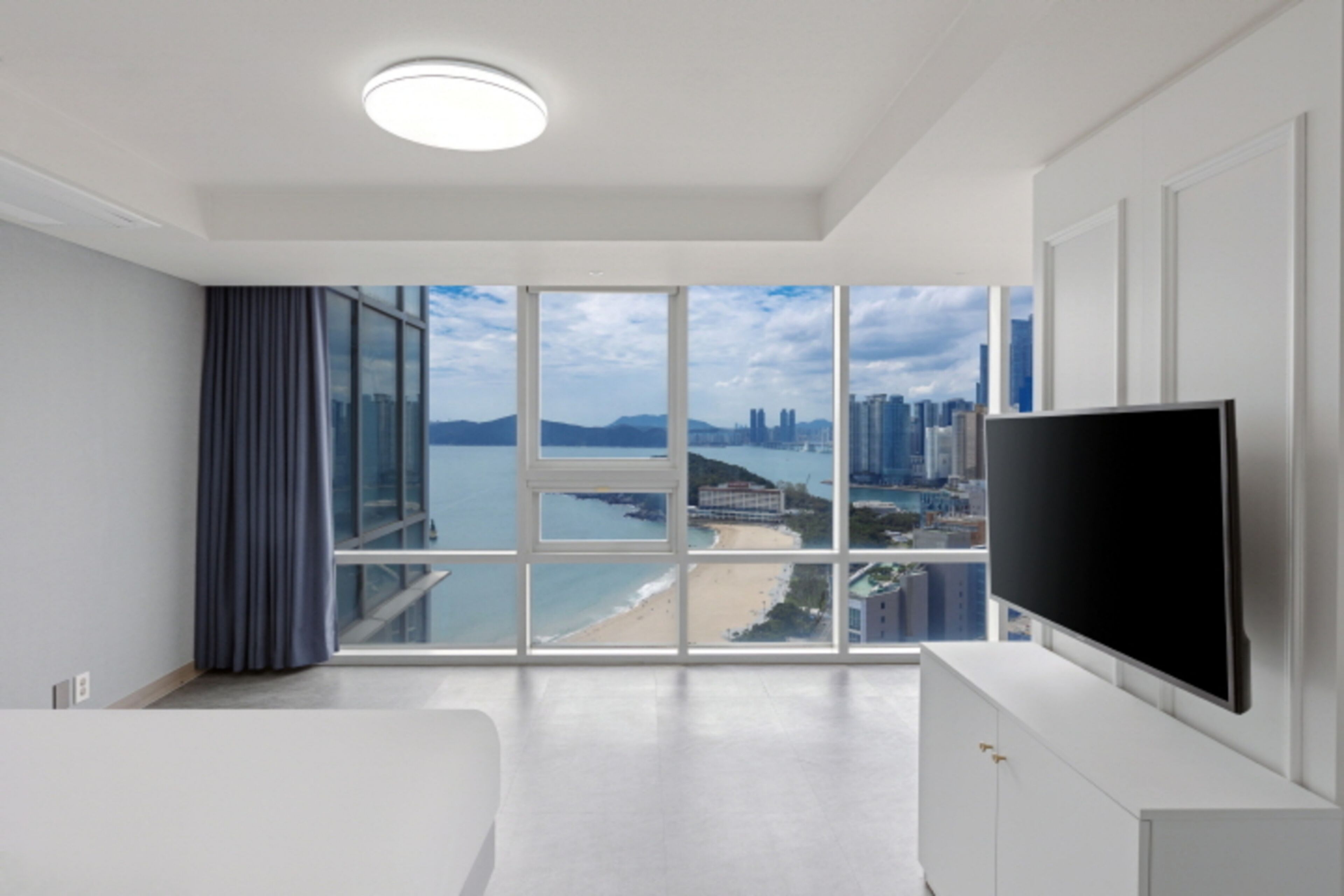 Quarto de hotel moderno com uma janela ampla, televisão de tela plana e uma cama branca.