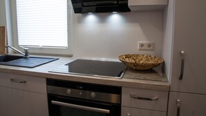 Uma cozinha com um fogão por indução preto, uma pia, uma tigela de madeira e eletrodomésticos de aço inoxidável.