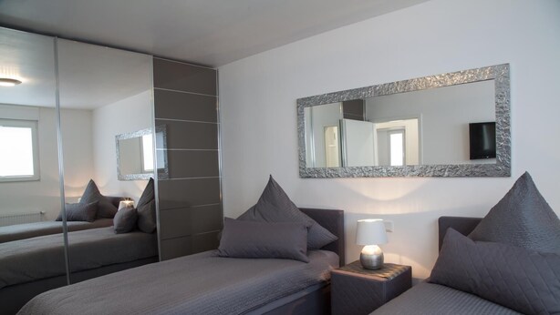 Quarto moderno com duas camas, um espelho grande e um abajur.