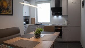 Uma cozinha moderna com área de jantar, destacando uma mesa de madeira, cadeiras, uma cafeteira e uma janela ampla que oferece luz natural.