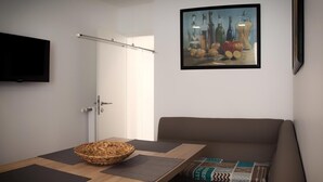 Uma sala de estar moderna com uma mesa de jantar de madeira, uma cesta de palha, um sofá marrom e um quadro com garrafas e abóboras na parede.