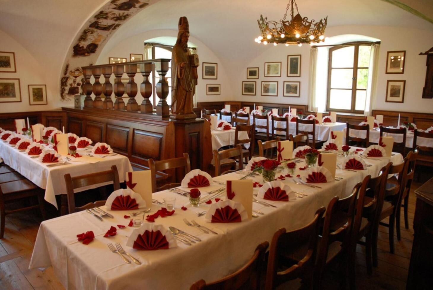 Salão de banquetes com mesas longas dispostas para um evento formal, com jogos americanos vermelhos e arranjos florais.