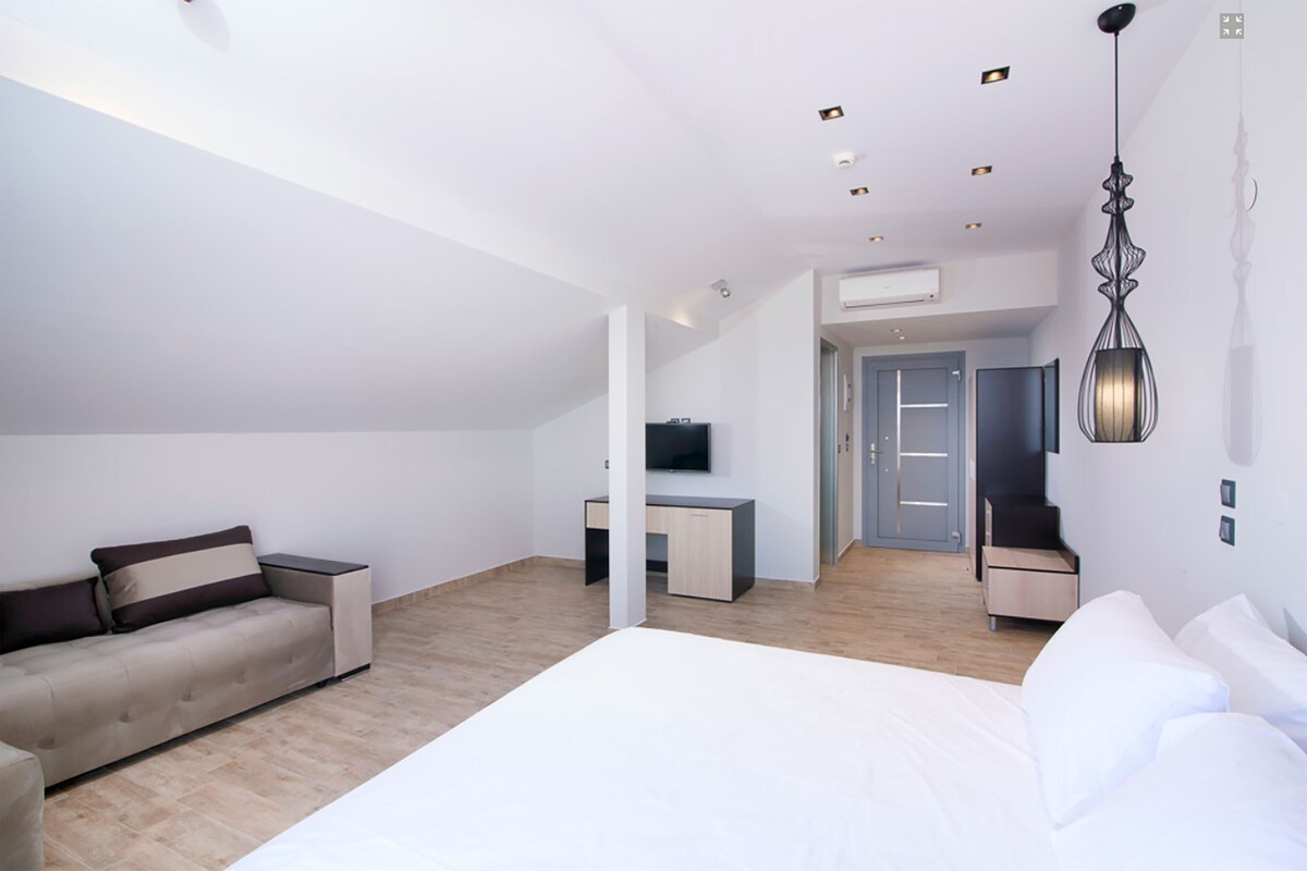 Quarto de hotel moderno com cama, escrivaninha, sofá e televisão.