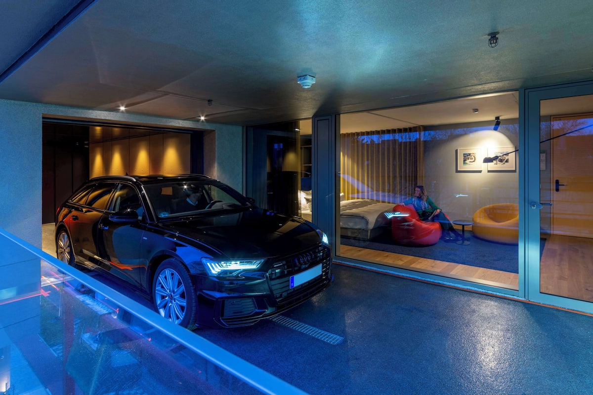 Um interior moderno com um carro estacionado na garagem, uma cama e uma poltrona de feijão vermelha.