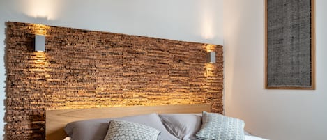 Quarto moderno com cabeceira em parede texturizada, estrutura de cama de madeira e duas almofadas estampadas.