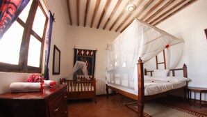 Quarto com cama de madeira, cômoda de madeira, janela com cortinas e tapete estampado.