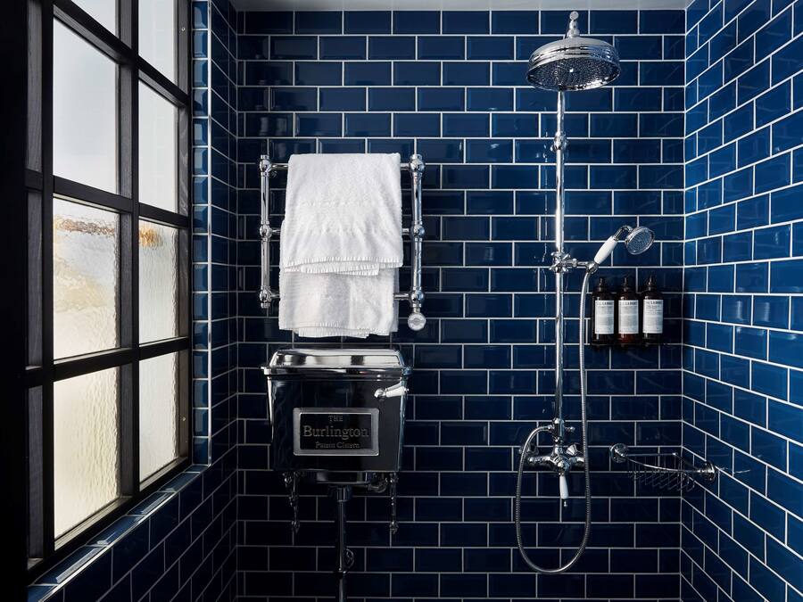 Casa de banho com parede azulejada em azul, toalha branca pendurada num suporte, sanita e chuveiro com cabeça de duche manual.
