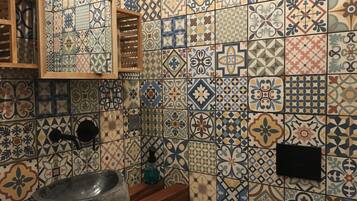 Um banheiro com uma bacia de pedra, uma prateleira de madeira e um revestimento de azulejos com diversos padrões.