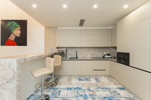 Uma cozinha moderna com bancada de mármore, forno embutido e máquina de café.