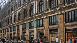 Um amplo espaço público interno, com pé direito alto, grandes janelas e detalhes arquitetônicos elaborados.