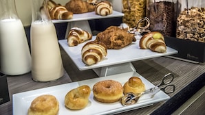 Um buffet de café da manhã com pães, leite e um par de tesouras em um suporte.