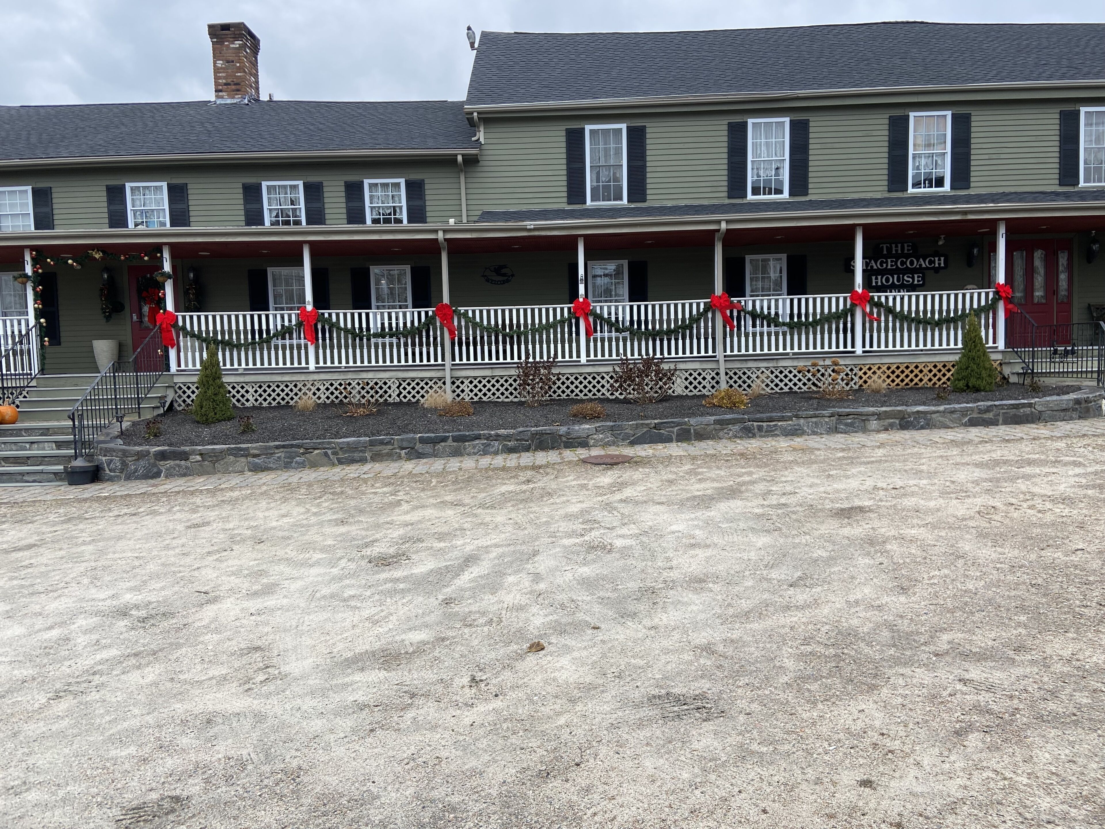 Um edifício com varanda decorada com laços e guirlandas vermelhas, uma placa com a inscrição "The Stagecoach House" e uma cerca de piquete branca.