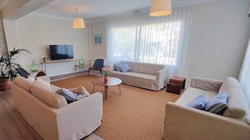 Uma sala de estar moderna com dois sofás, uma mesa de centro, uma televisão e uma janela grande com cortinas.