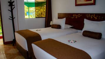 Quarto de hotel com duas camas, cabeceira de madeira com design floral, janela com vista para vegetação e um quadro na parede.