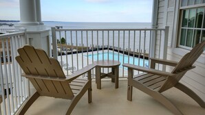 Varanda com duas cadeiras Adirondack e uma mesa pequena, com vista para uma piscina e o oceano.