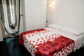 Quarto com cama, cortinas brancas e luminária fixada na parede.