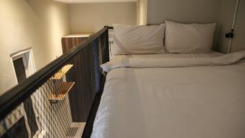 Quarto de hotel com uma cama, cabeceira de madeira, uma prateleira pequena e uma janela com vista para o exterior.