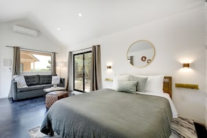 Quarto moderno com uma cama grande, um sofá e uma mesa de jantar. Há uma porta de vidro deslizante que dá para uma área externa.
