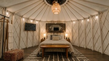 Quarto com tenda, cama, luminárias de cabeceira, um lustre e uma obra de arte emoldurada na parede.