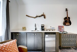 Cozinha compacta com máquina de lavar louça, cafeteira e um violão na parede.