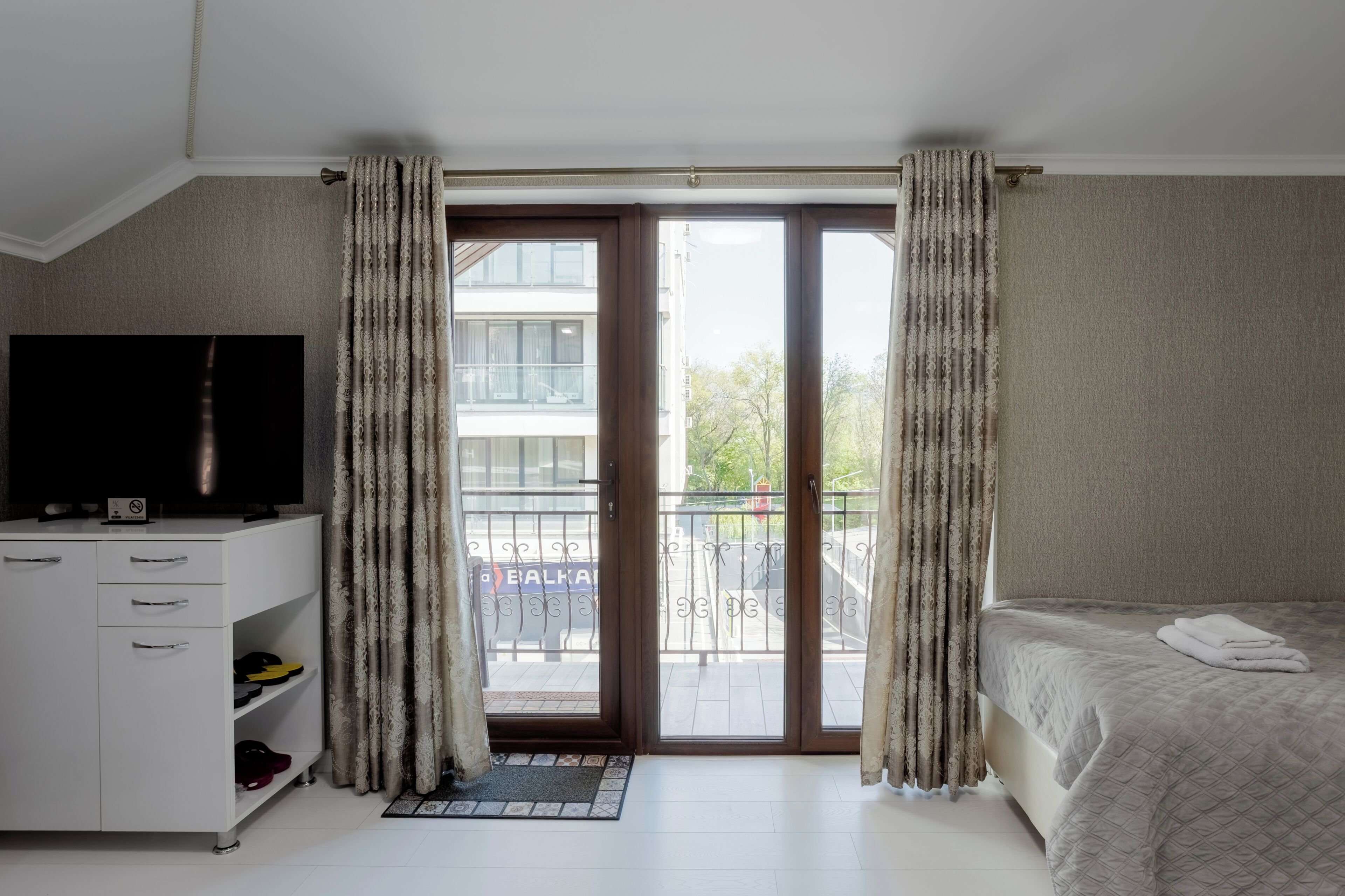 Quarto com cama, TV, guarda-roupa e varanda com grades.