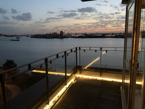 Varanda com guarda-corpo com vista para a paisagem urbana à beira-mar ao entardecer.
