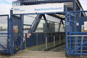 Um portão de metal azul com uma placa que diz 'Royal Arsenal Woolwich' e 'mbna Thames Clippers'.