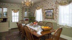 Uma sala de jantar com mesa de madeira, cadeiras, um candelabro e papel de parede com padrão floral.
