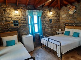 Quarto de paredes de pedra com duas camas, um relógio e uma janela com cortinas.