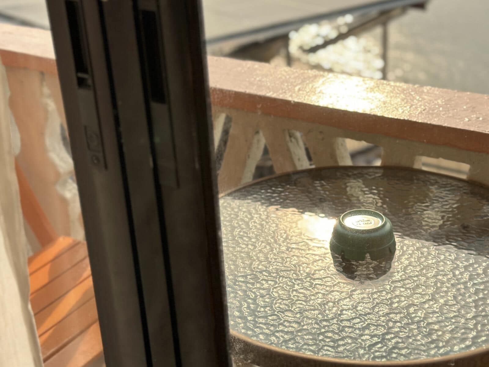 Uma mesa de vidro com uma garrafa, um corrimão de metal e um chão de madeira.