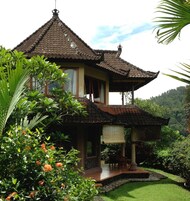 Uma casa tradicional com telhado de telhas, varanda e jardim com plantas tropicais.