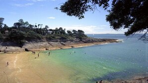 Uma praia com águas cristalinas, margem rochosa e algumas pessoas a nadar.