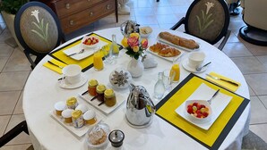 Mesa de jantar redonda posta com itens de café da manhã, incluindo croissants, frutas e acompanhamentos.
